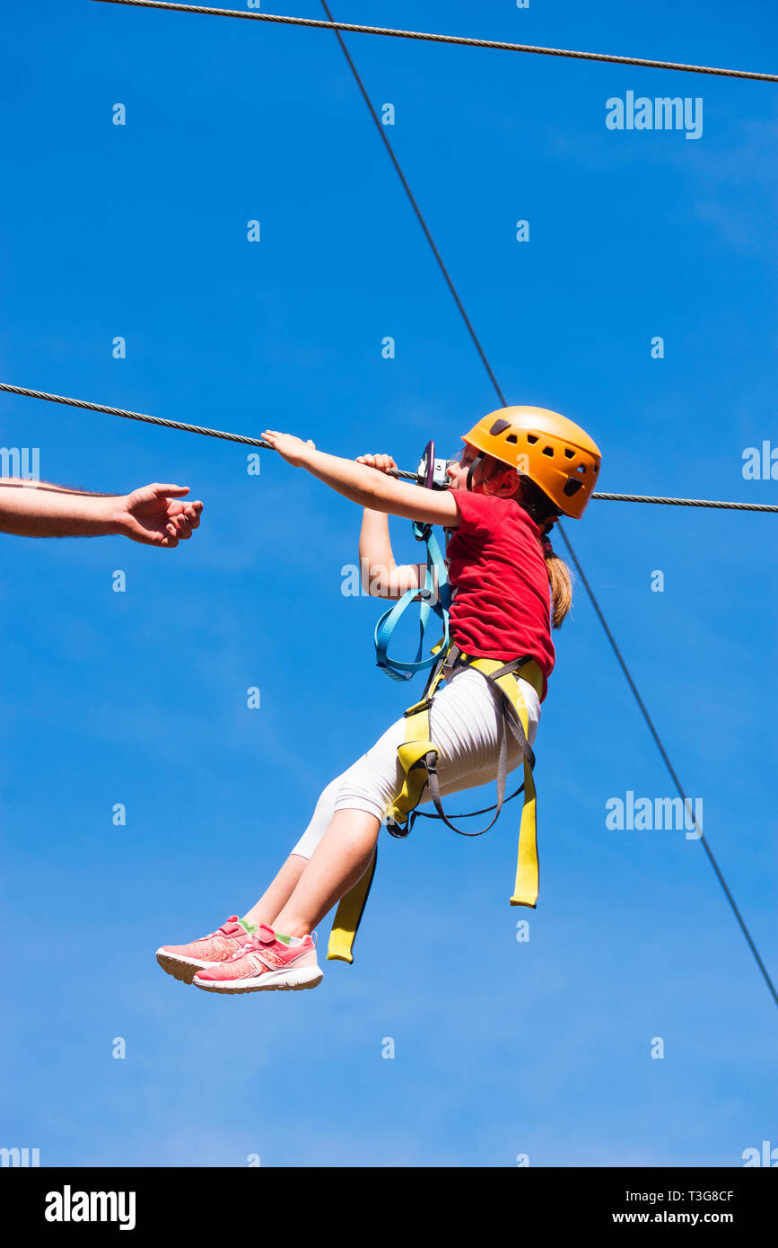 Little brave caucasian girl using a zip line. An indefinited man lend a ...