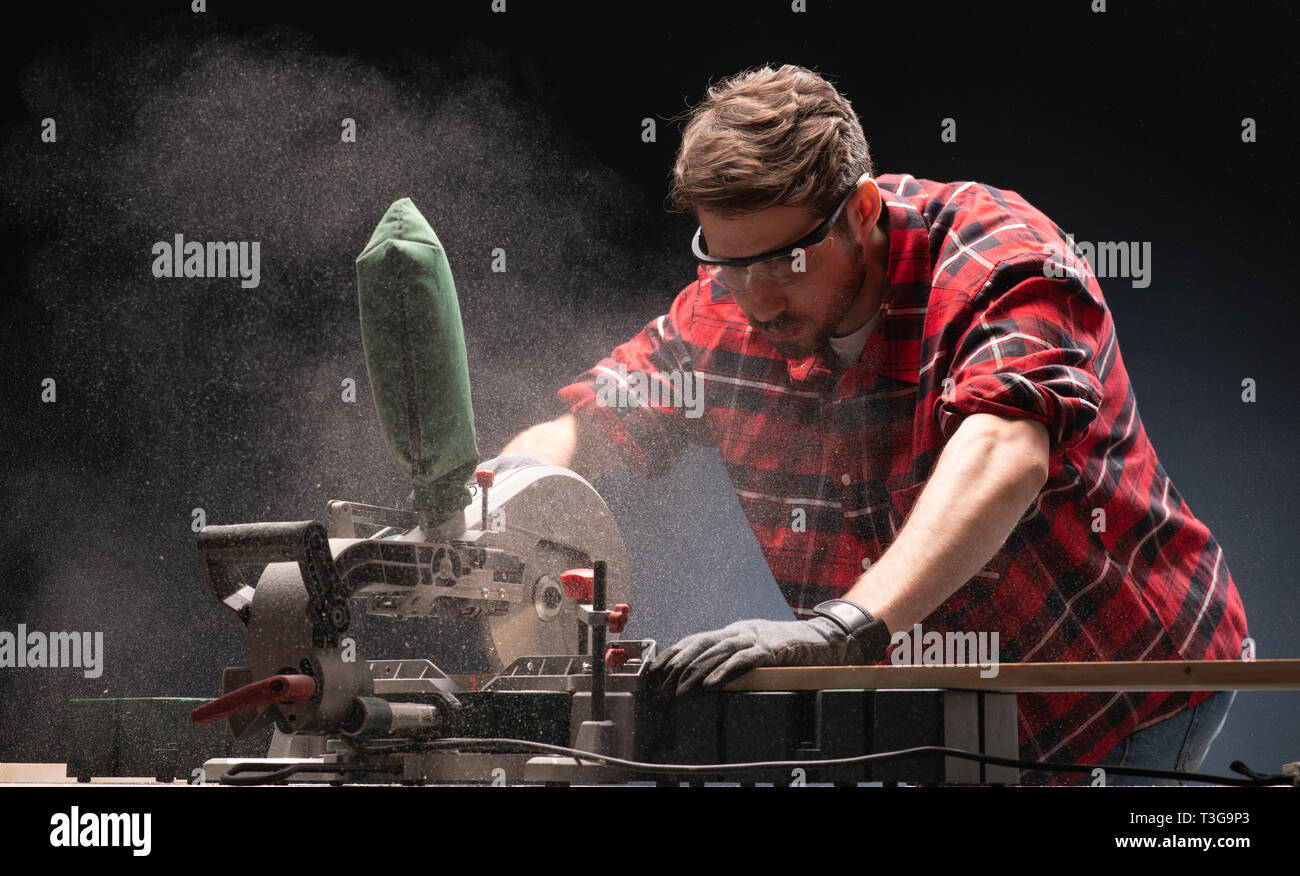Handsome man using modern electric circular saw for ctting wood in the ...