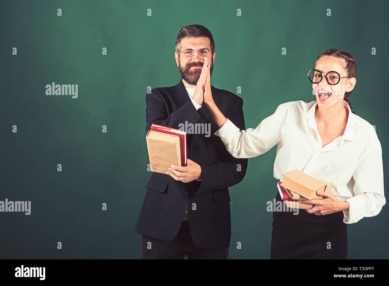 Two students clap hands together with bookd on green blackboard ...