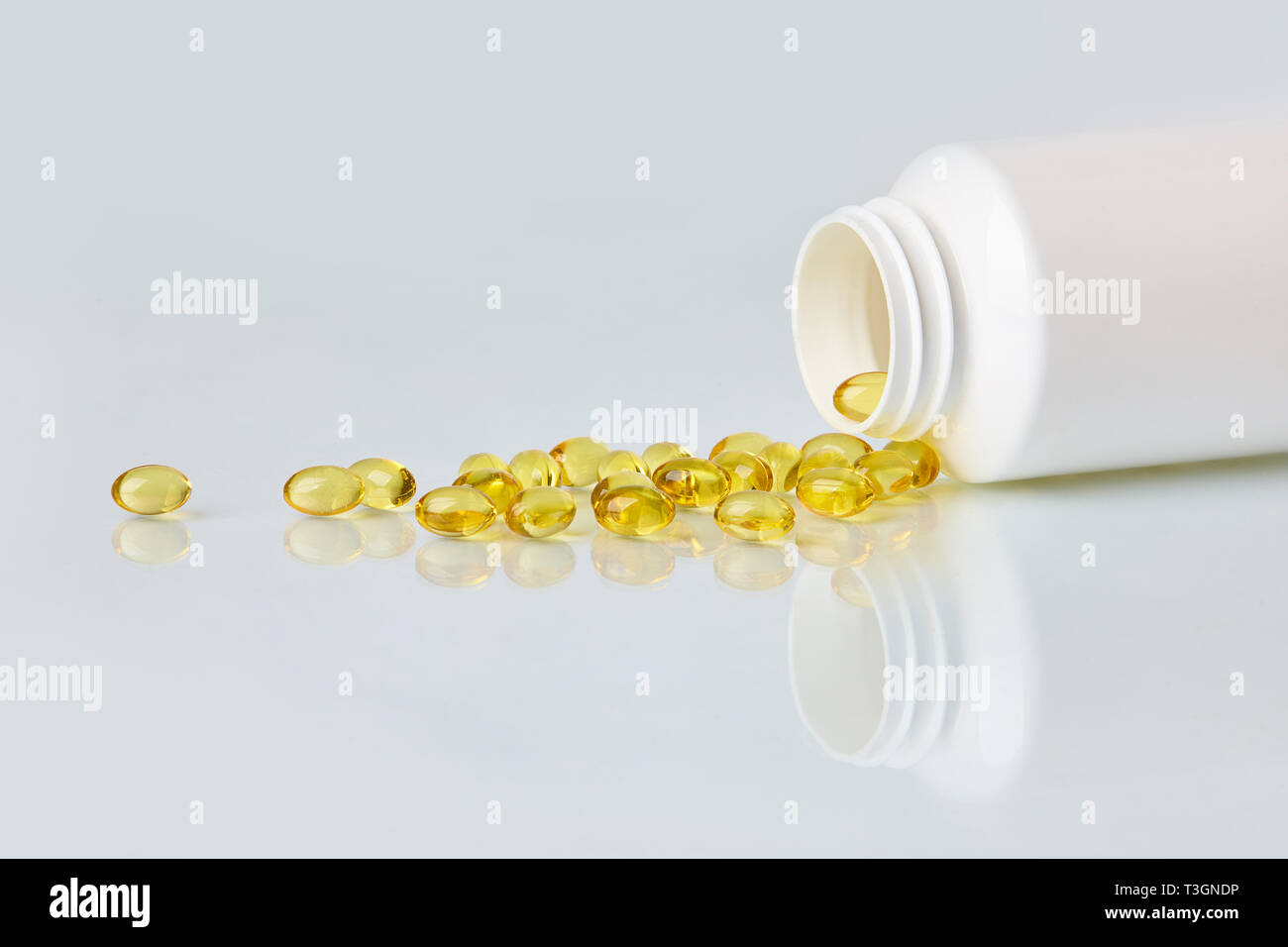 Fish oil capsules scattered from white plastic bottle on white ...