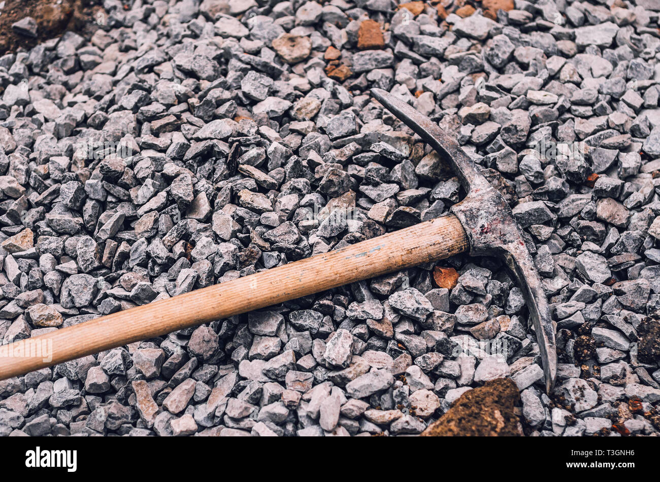 Metal pickaxe on a wooden handle on a pile of small rubble. Dirty hard ...