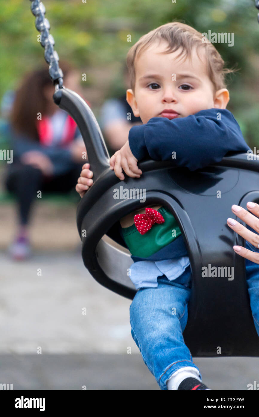 Baby boy with puzzled face holding to a swing on outdoor playground ...