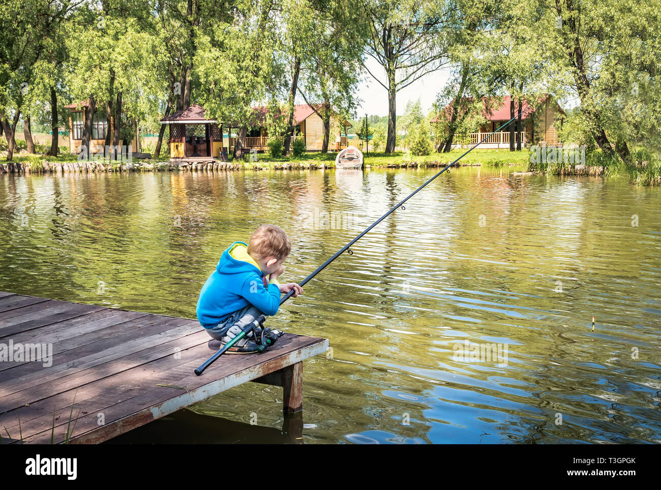 Boy fishing from a wooden dock on a lake or pond pier in a sunny summer ...