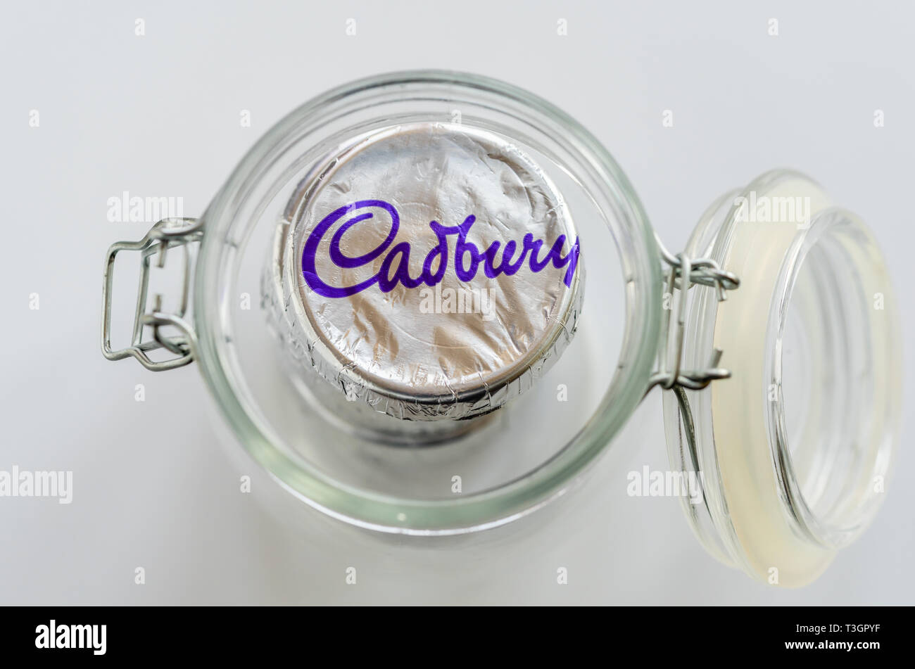 Round Cadbury biscuits wrapped in silver foil in an open glass jar ...