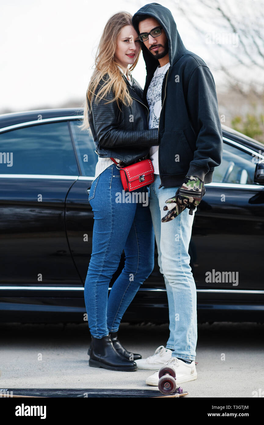 Cool multiracial couple hugs together with longboard against black ...