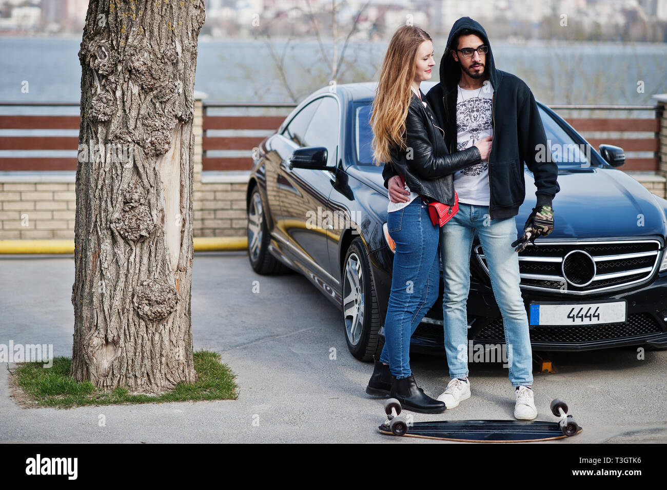 Cool multiracial couple hugs together with longboard against black ...