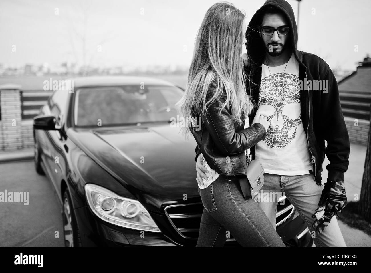 Cool multiracial couple hugs together against black elegant sport car ...