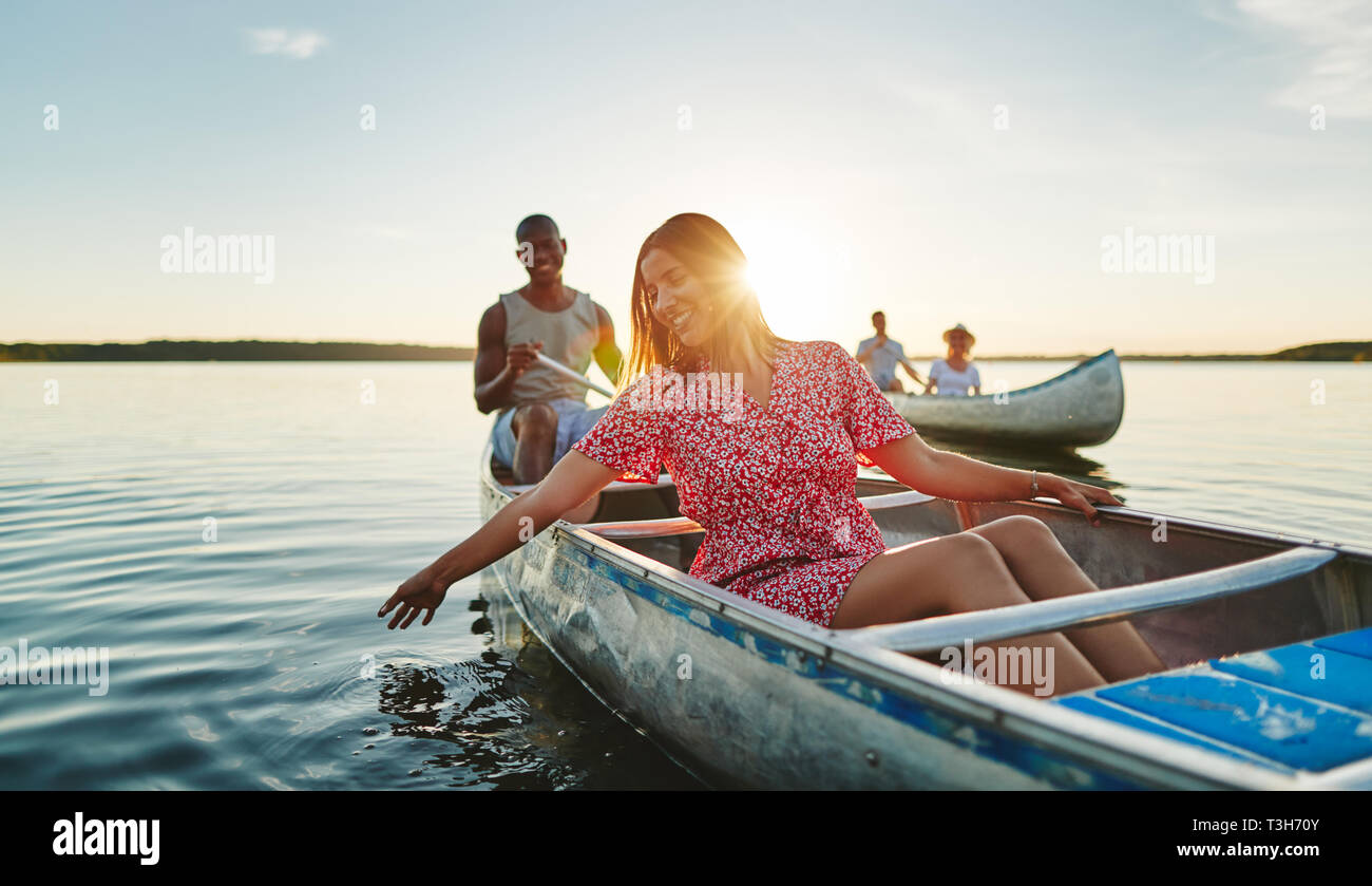 Smiling young woman dipping her hand in lake water while paddling a ...