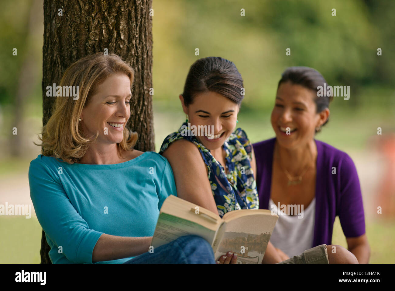 Happy friends reading a book together under a tree at the park Stock ...