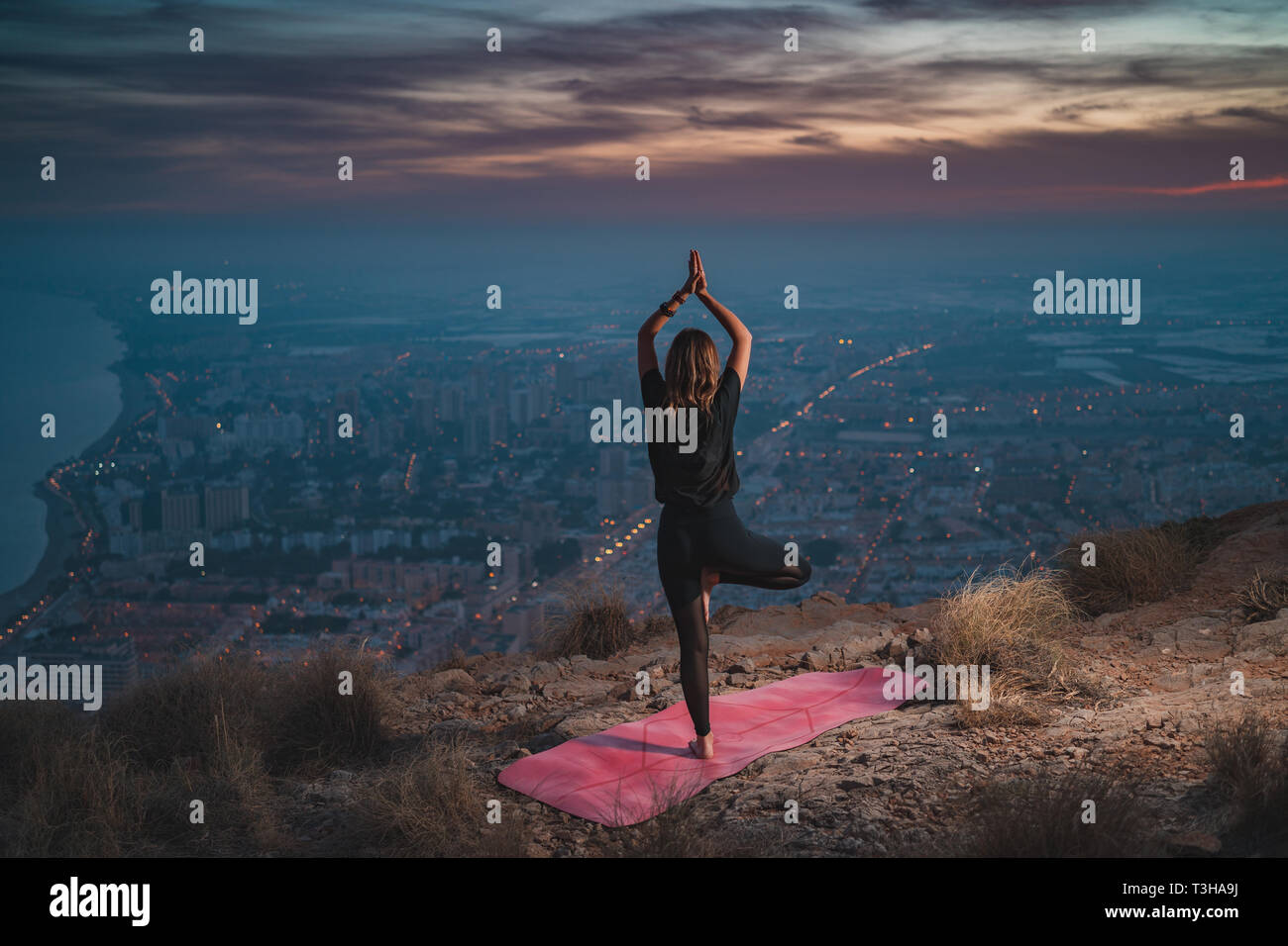 Beautiful young woman doing yoga at the top of the mountain with views ...