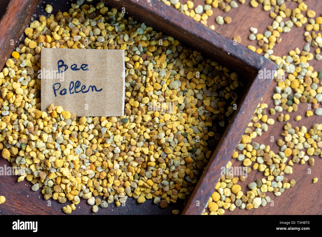 small wooden box containing bee pollen, on a dark wooden table with ...