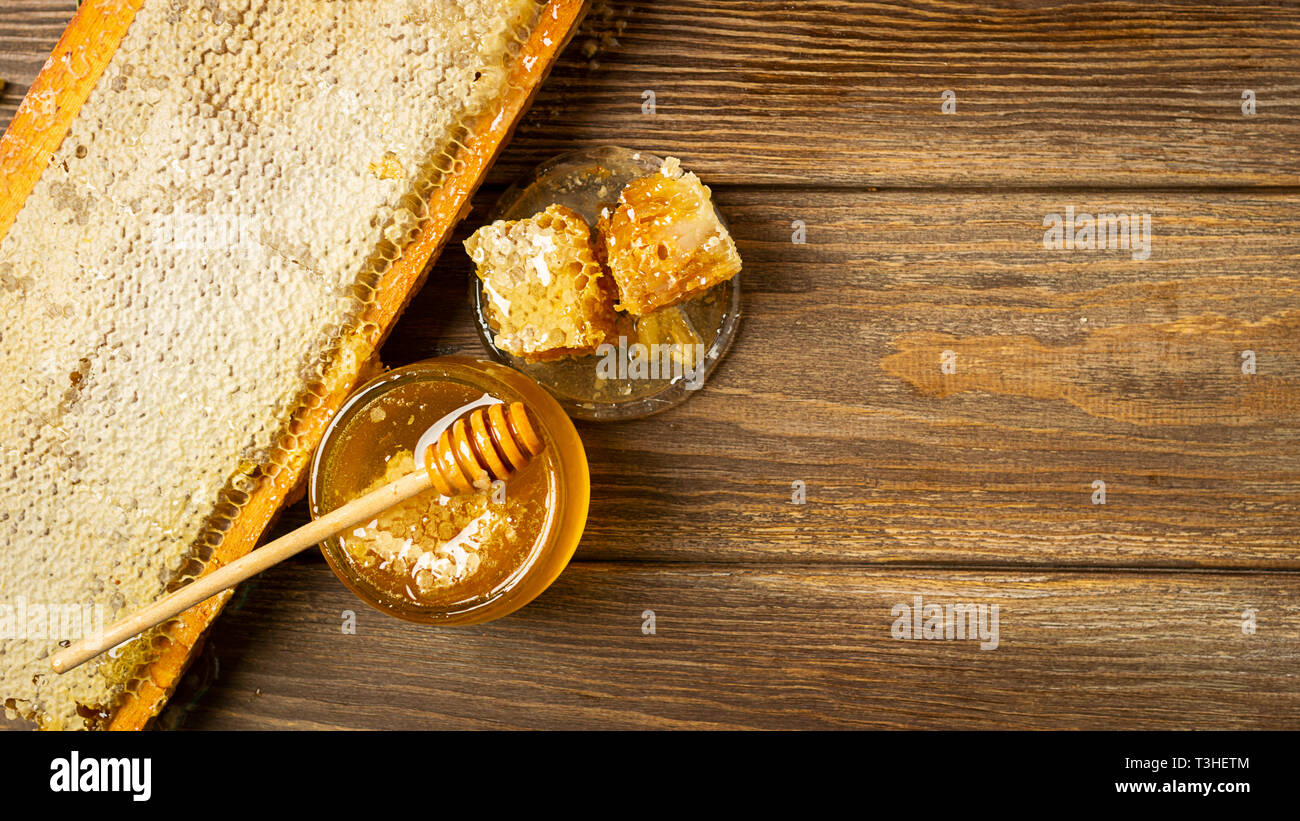 Golden fresh honey in a glass jar and honeycombs on a wooden table. The ...