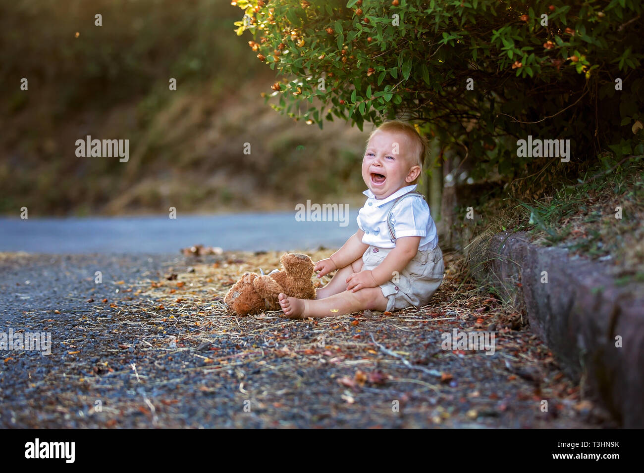 Sad little toddler boy, holding teddy bear, sitting lonely on a road in ...