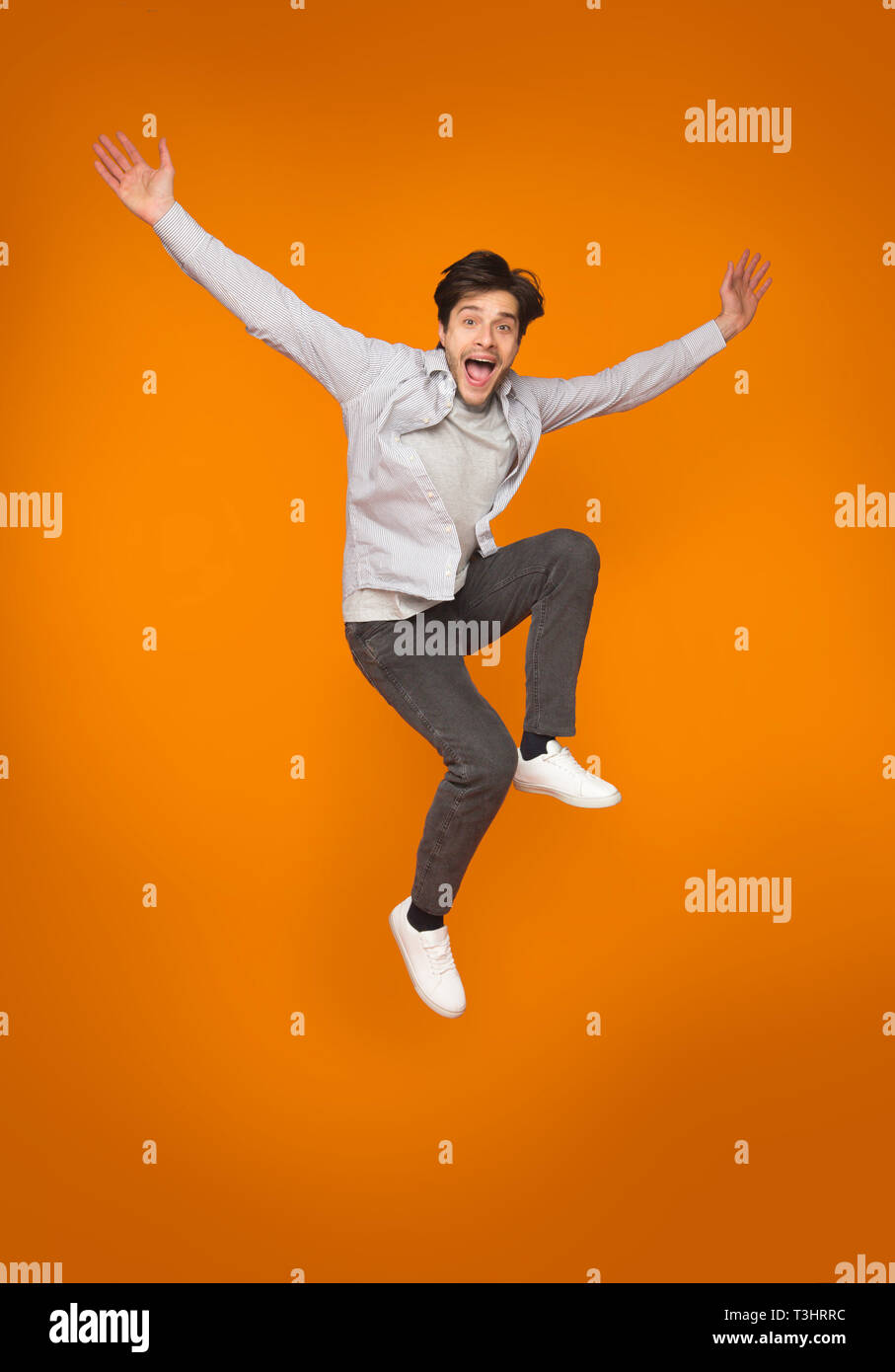 Funny man jumping with raised arms over orange background Stock Photo ...