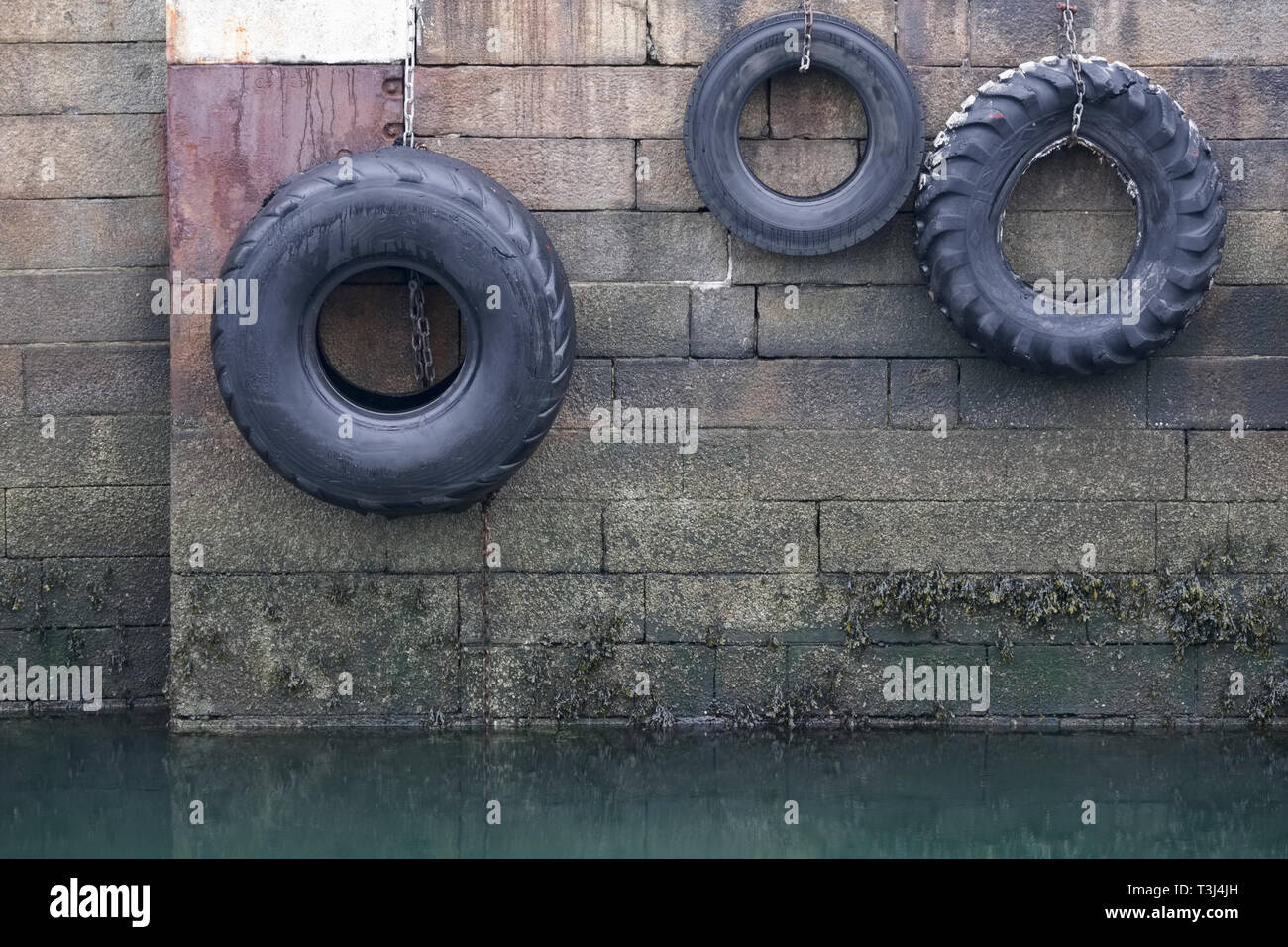 Car tyres hanging on rope against harbour wall at port dock to protect ...