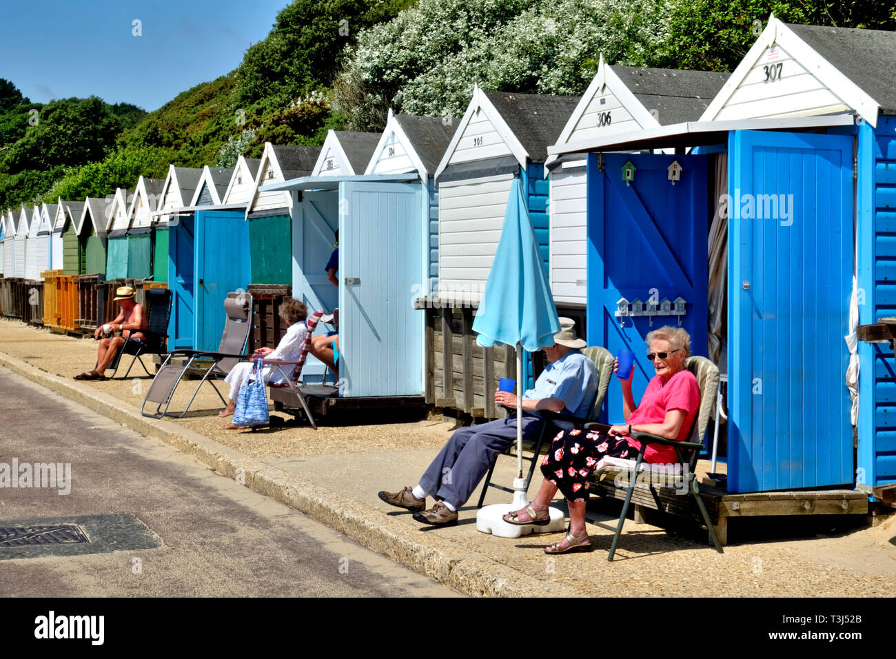 People relax and enjoy the sunshine in front of the beach huts along ...