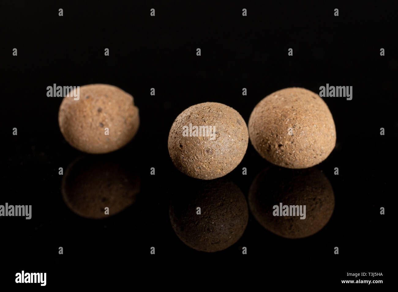 Group of three whole brown clay pebbles (leca) isolated on black glass ...