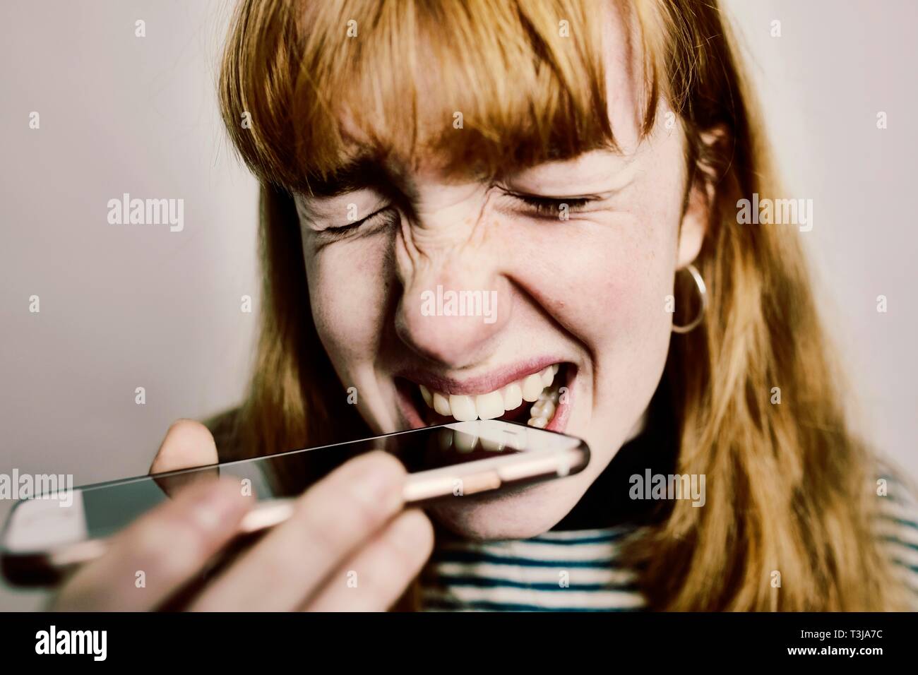 Girl, teenager, redheaded, biting into her smartphone out of ...