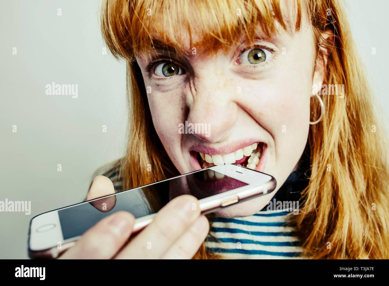 Girl, teenager, redheaded, biting into her smartphone out of ...