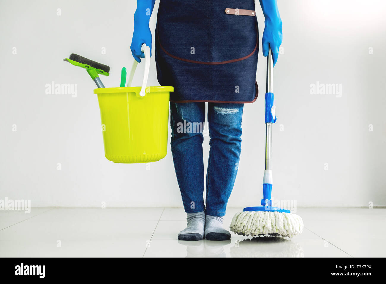 Young housekeeper cleaning floor mobbing holding mop and plastic bucket ...