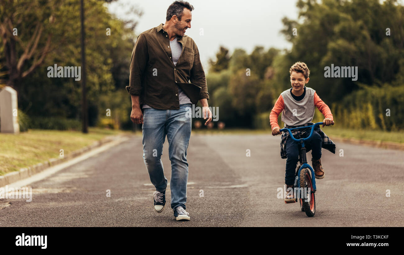 Boy riding a bicycle while his father walks along. Kid learning to ride ...