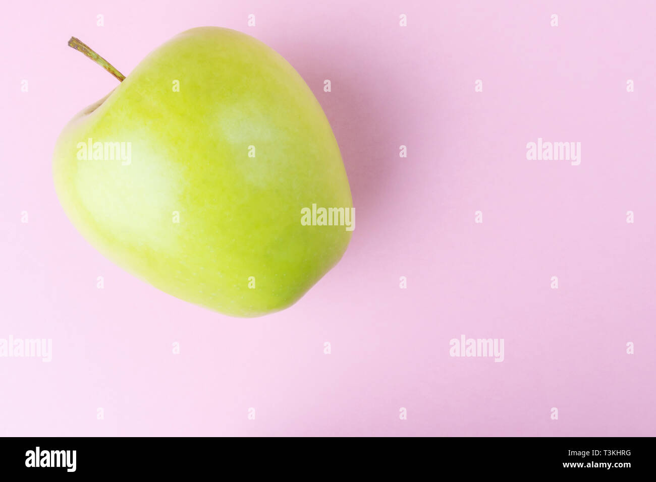 Fresh green-yellow apple close-up on the background of a pastel pink ...