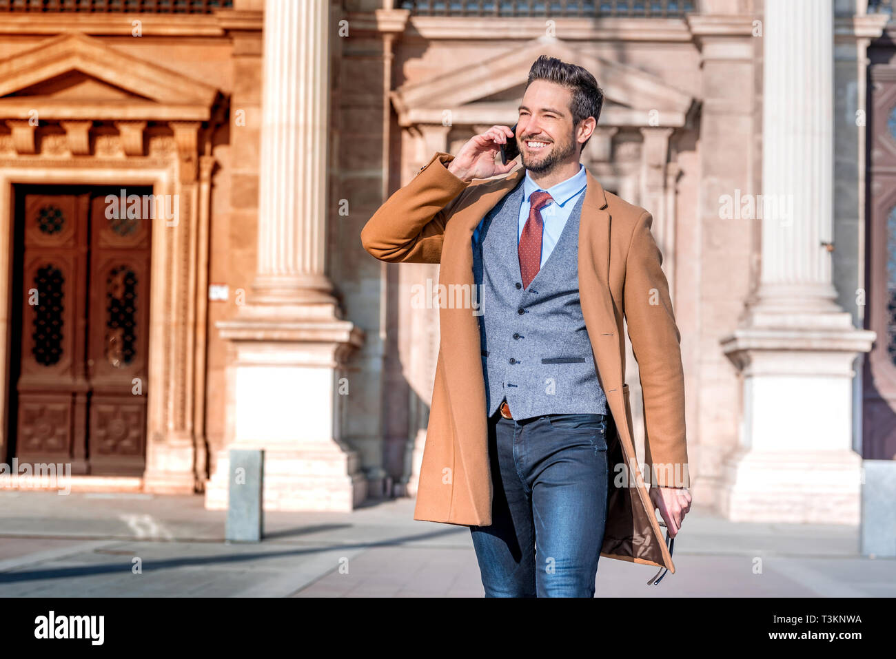 A handsome elegant man standing on a square and using his smartphone on ...