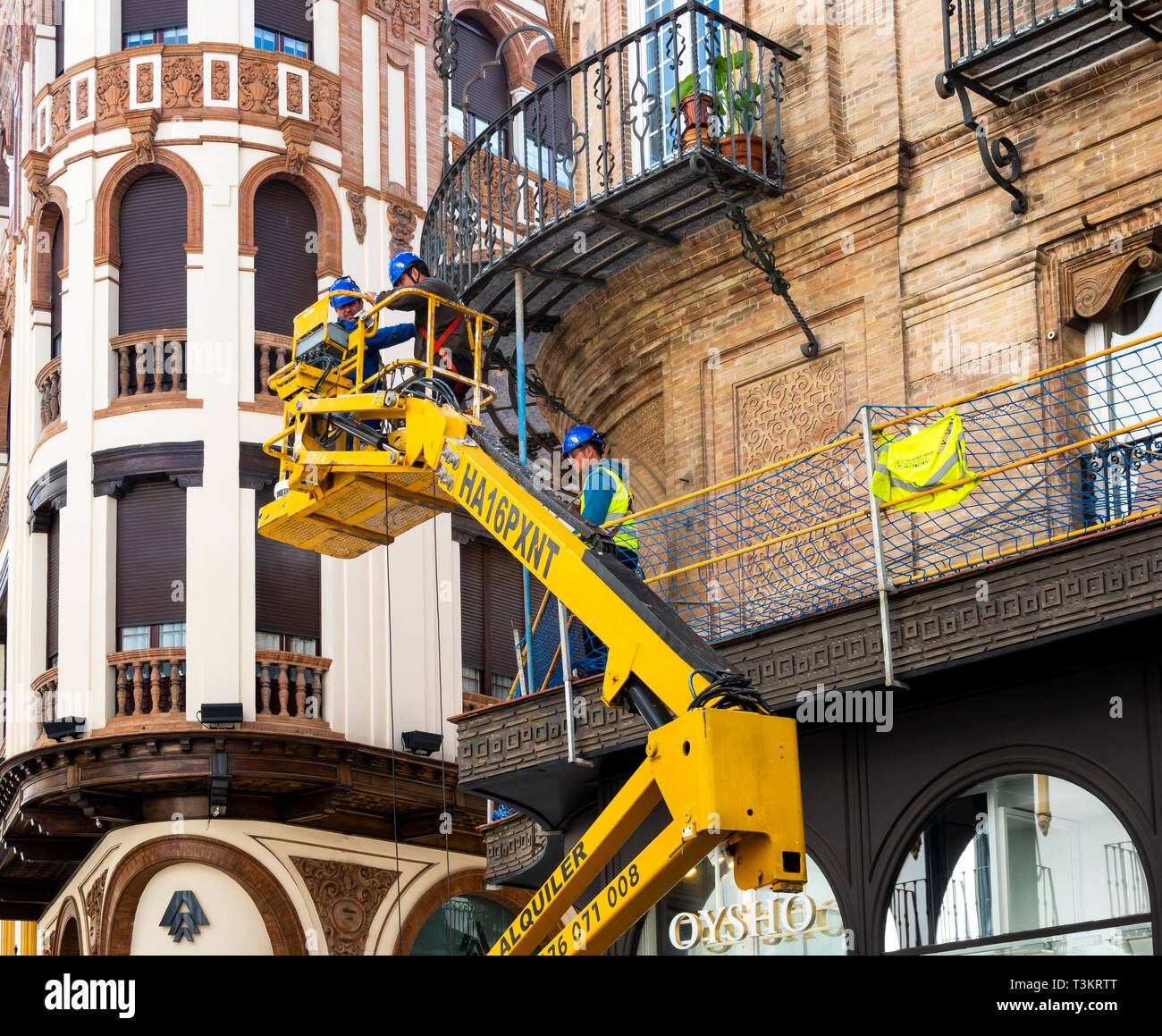 Three men on a Houlotte HA 16 PX boom hoist repairing a metal balcony ...