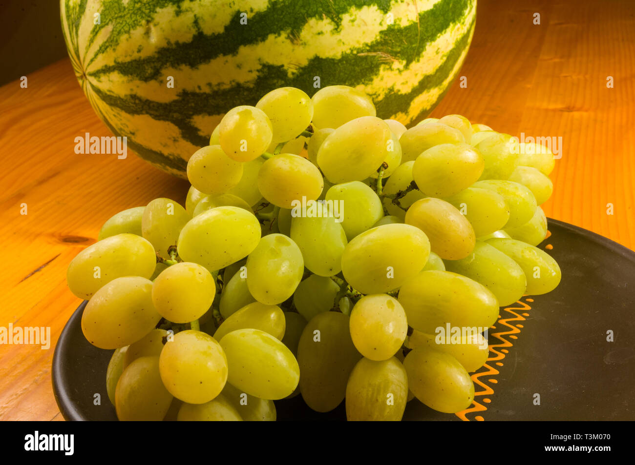 still life - a large brush of green grapes and watermelon in a dark ...
