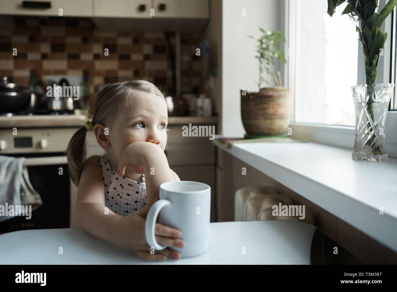 Little cute girl sitting at the table in the kitchen Stock Photo - Alamy