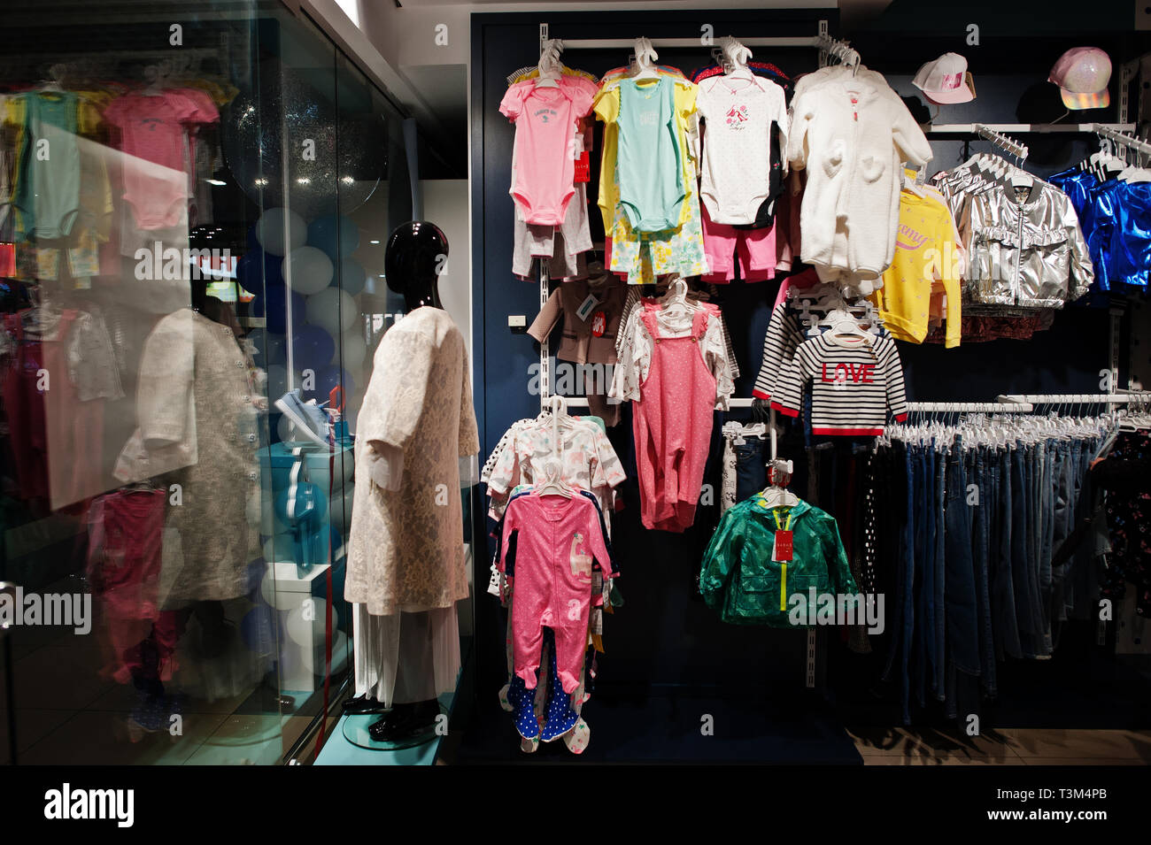 Children's bright clothes hang on the display in the baby clothing ...