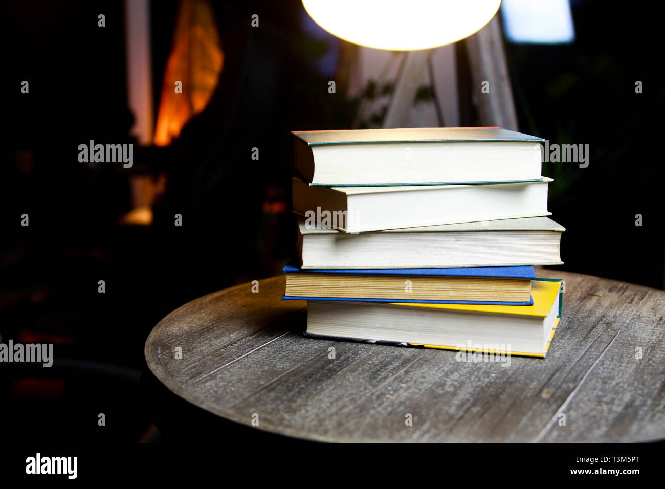 Stack of old books on round wood table with reading light during night ...