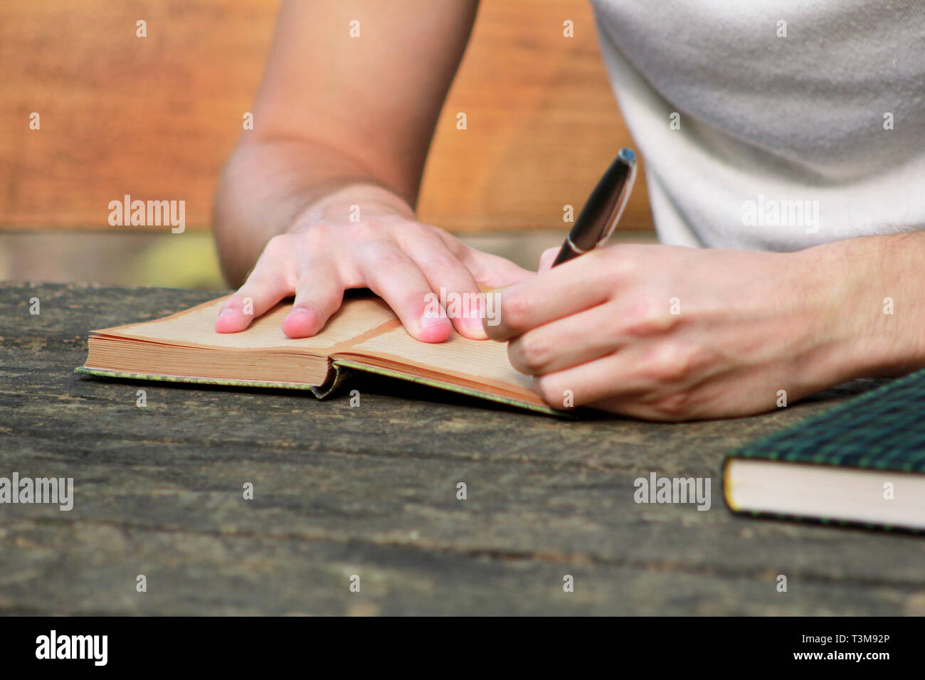 Young handsome guy sitting at wooden table, writing a book, doing ...