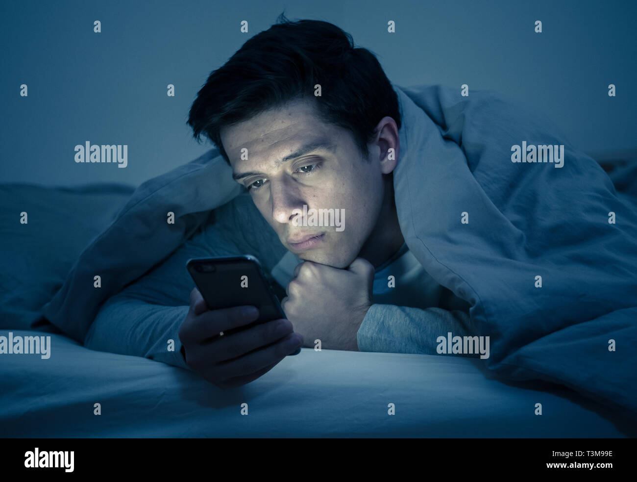 Young mobile phone addict man awake at night in bed using smartphone ...