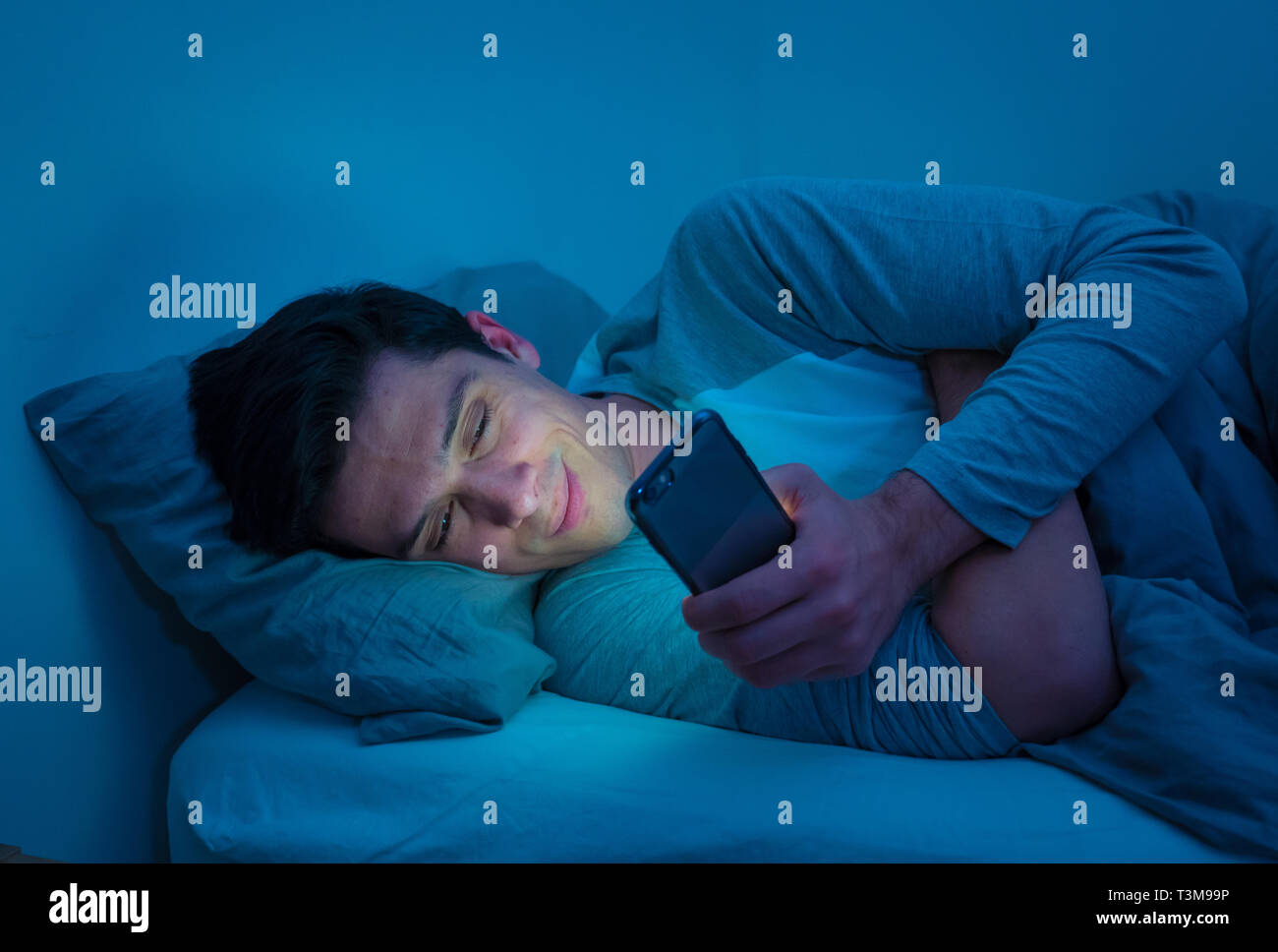 Young mobile phone addict man awake at night in bed using smartphone ...