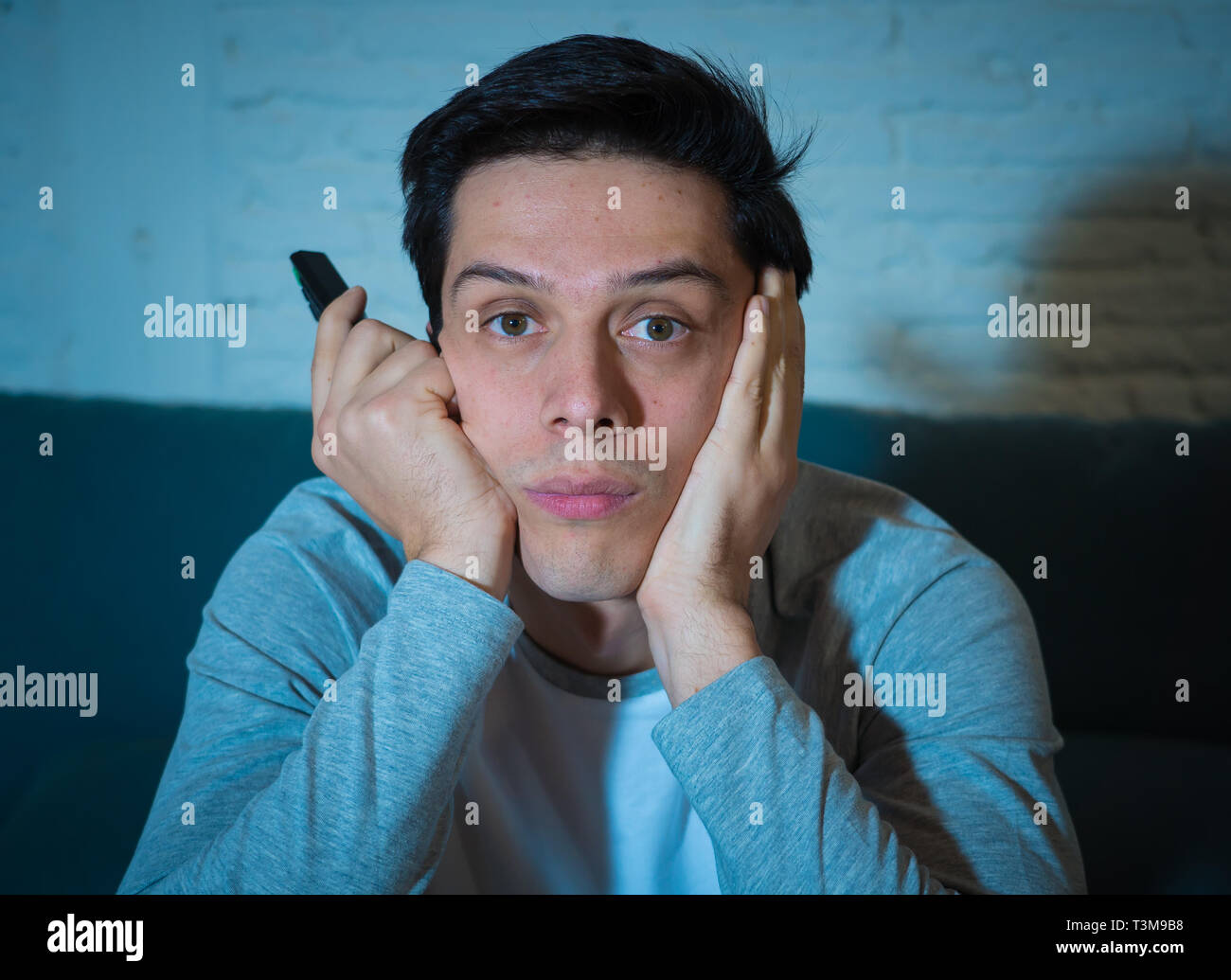 Young bored man sitting on couch using remote control zapping for ...