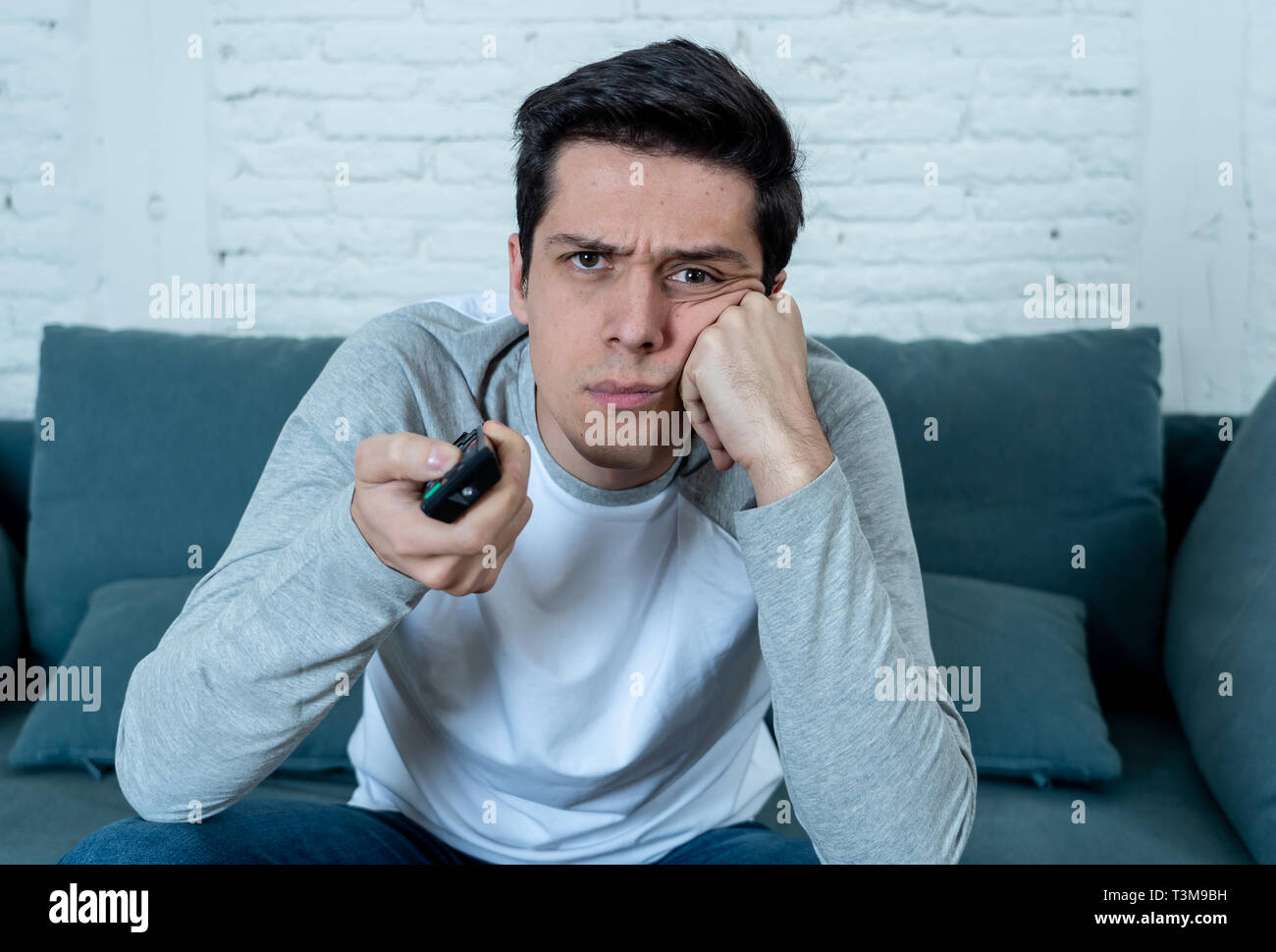 Lifestyle portrait of young bored man on couch with remote control ...