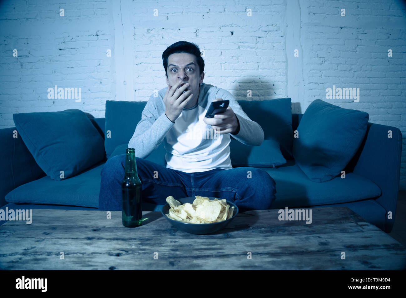 Lifestyle portrait of young scared man watching horror movie or ...