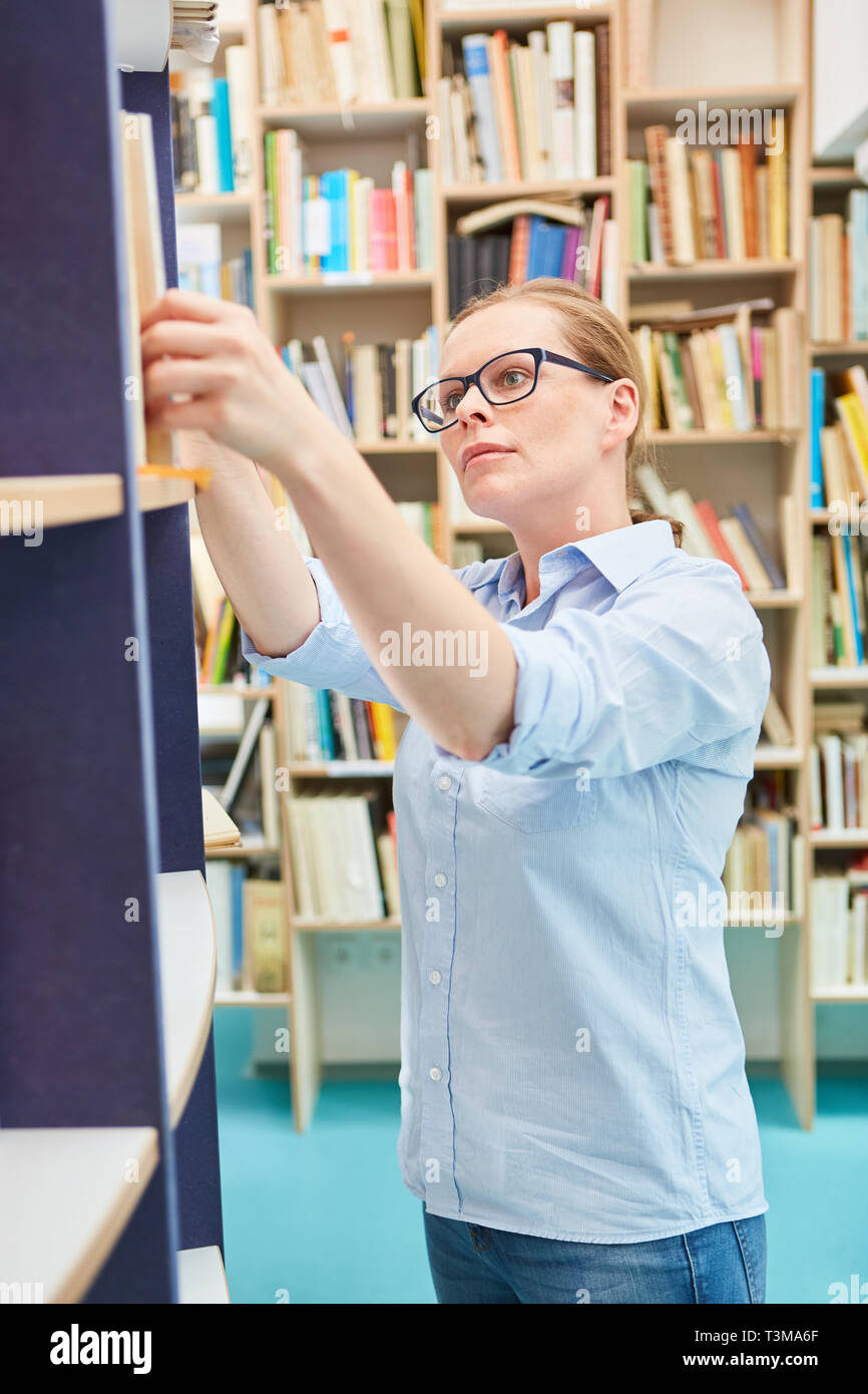 Woman as a bookseller or librarian searches for a book on the shelf of ...