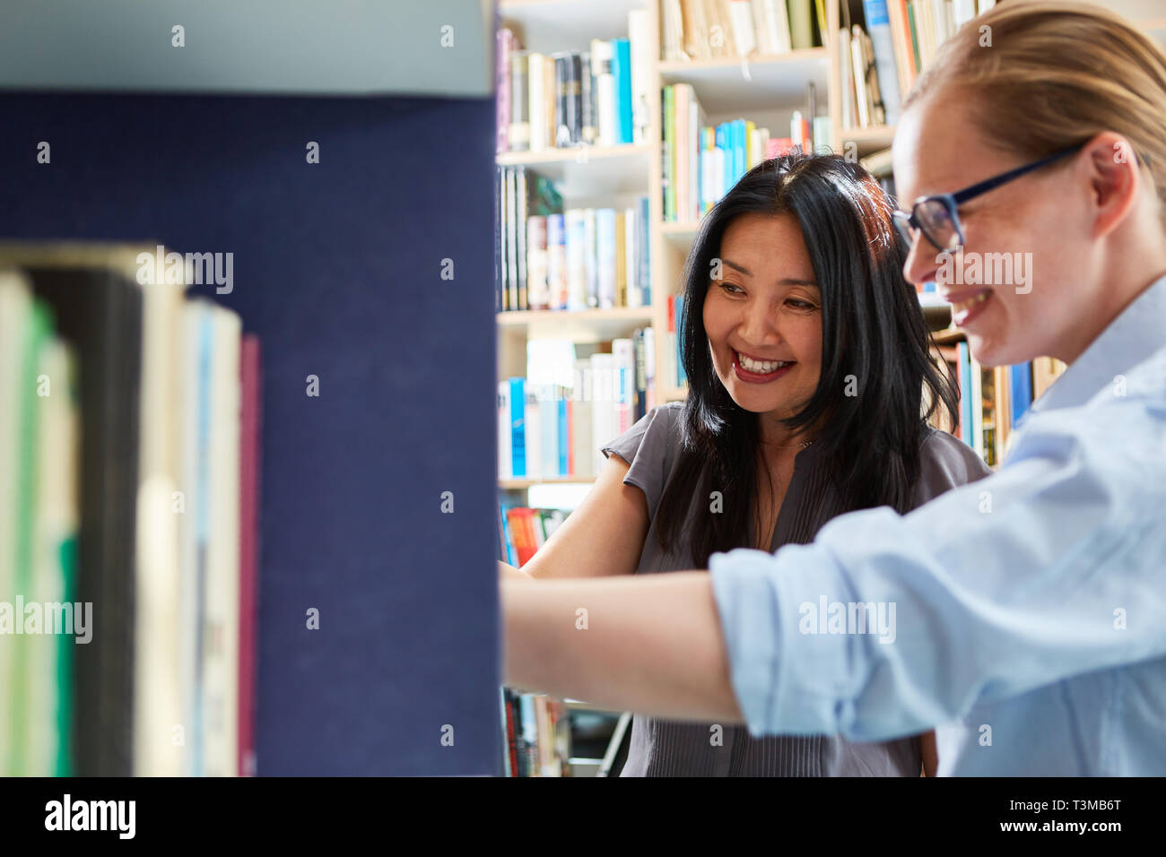 Two women are looking together for a book on the shelf in the library ...