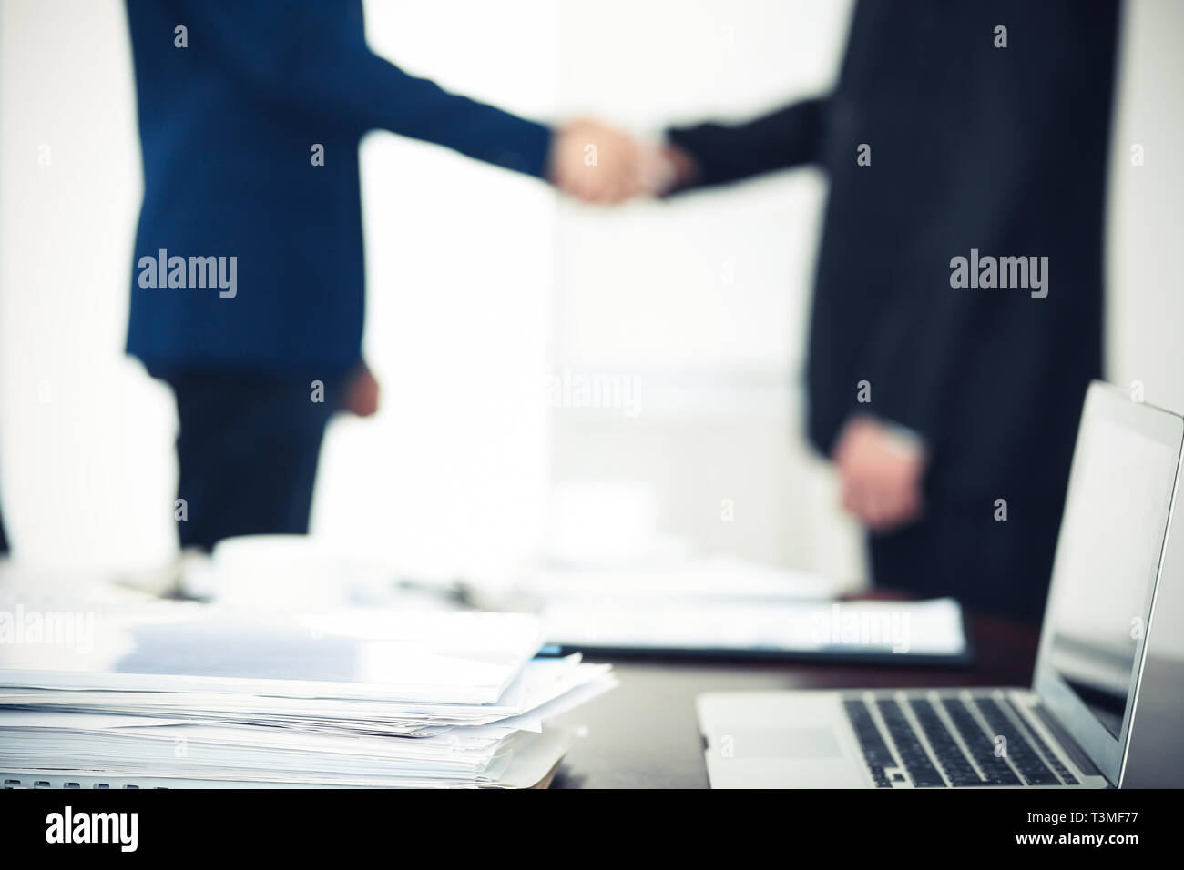 Documents and laptop on the table. Business people shaking hands on the ...