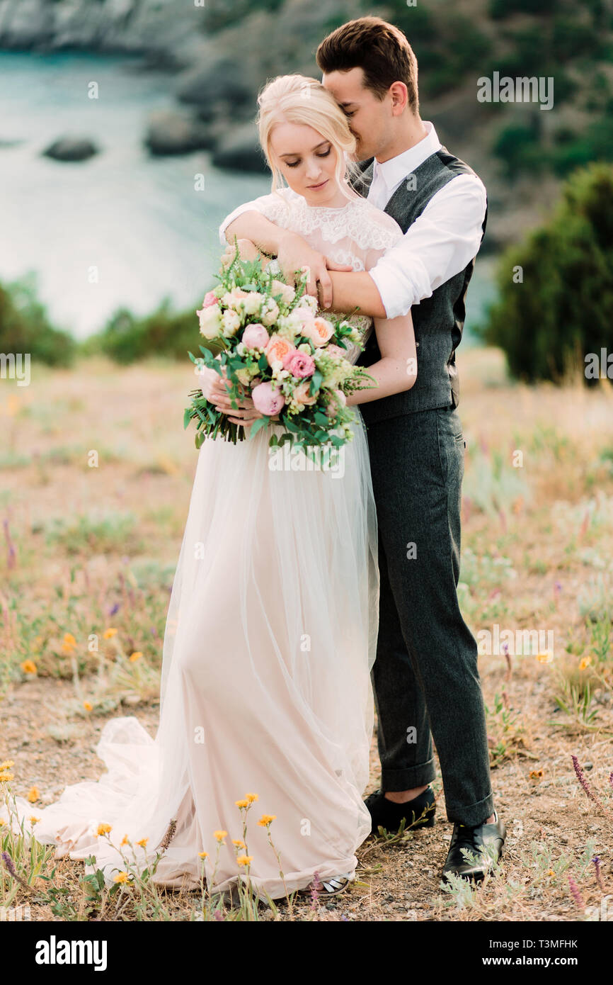 Beautiful bride and groom hug each other tender standing on the golden ...