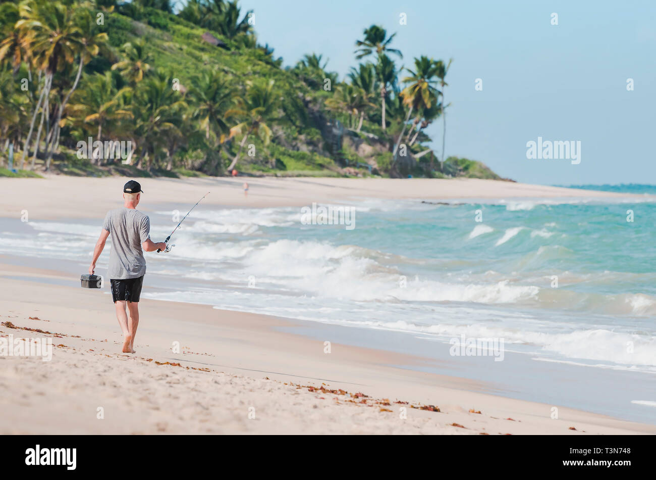 Fisherman holding a fishing rod walking on the beach. Man walking on ...