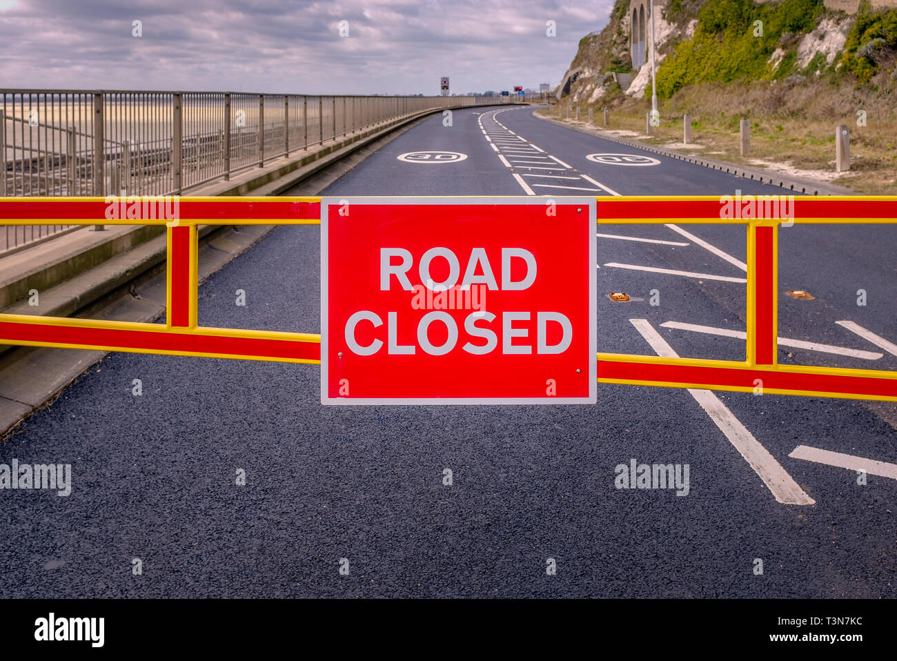 Red road closed barrier across an empty tarmac road with white road ...