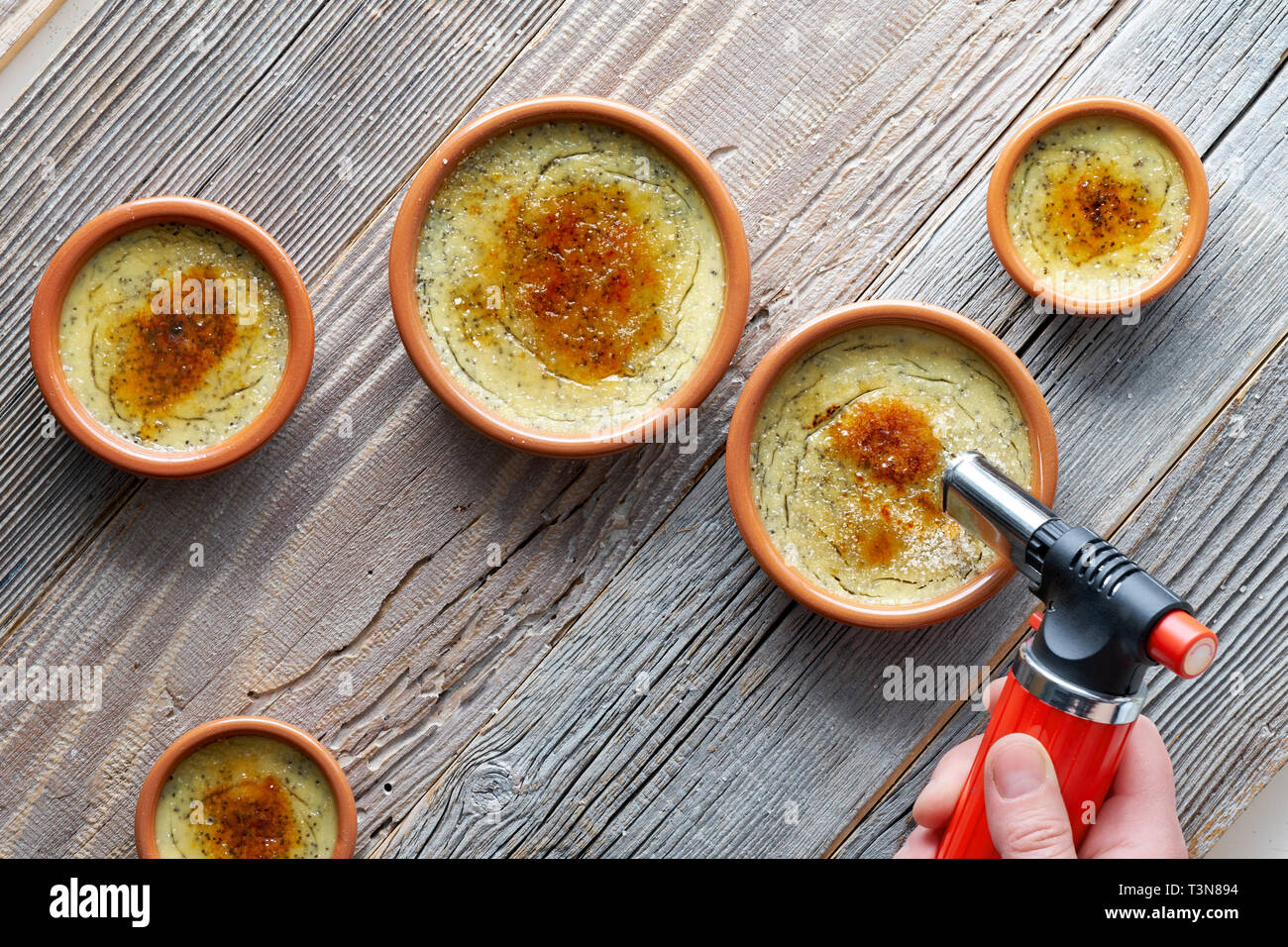 Making creme brulee. Flat lay on rustic wooden table with ceramic brown ... Making creme brulee. Flat lay on rustic wooden table with ceramic brown ...
