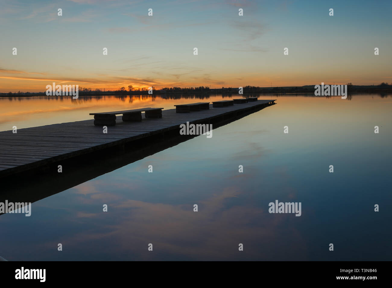 A long bridge with benches, a sunset and a calm lake - evening beauty ...