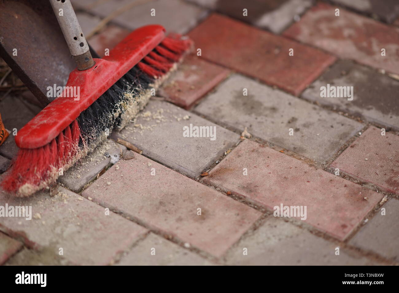 Red plastic broom clogged with sand standing on the tile. Place for ...