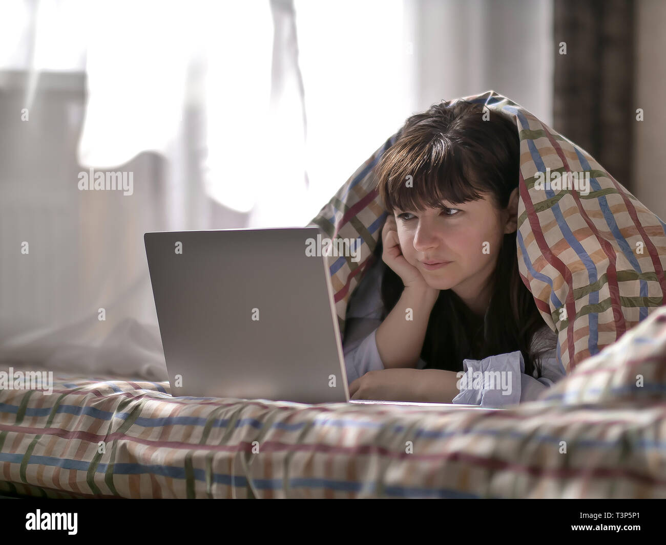 Cute brunette girl is lying under the covers and looking into the ...