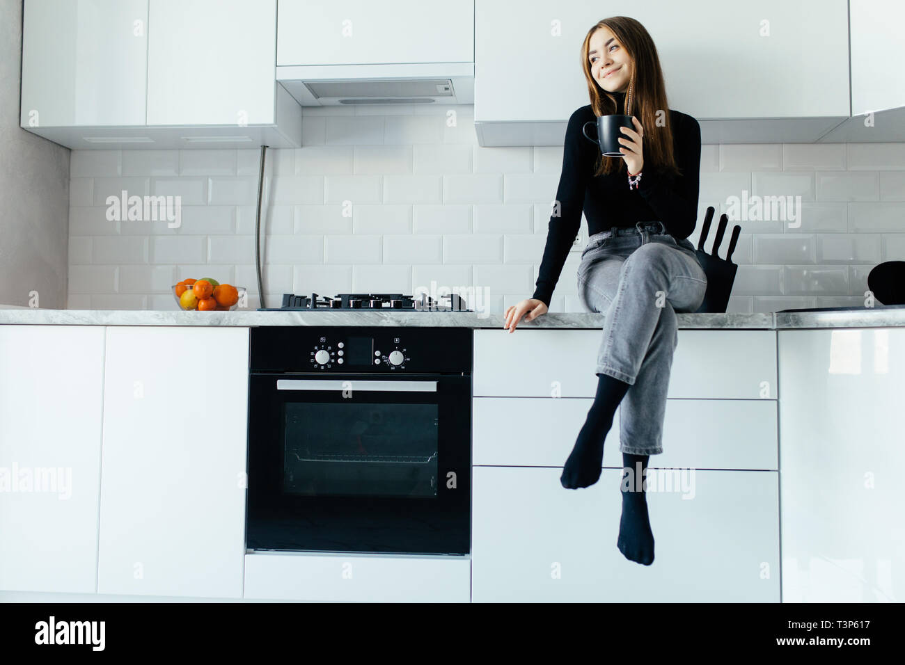 A young woman moving in new home, sitting on a counter in the kitchen ...