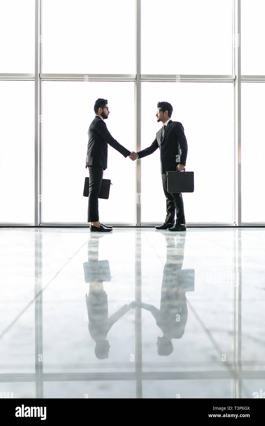 Full length side view of businessmen shaking hands in office building ...